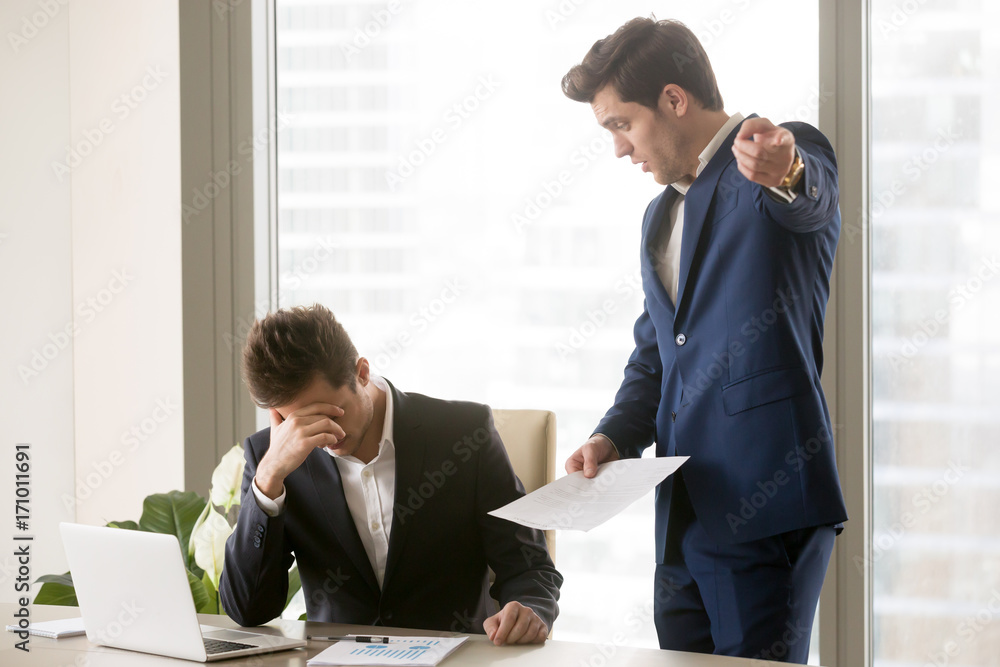 Boss criticizing frustrated male employee because of mistakes in report ...