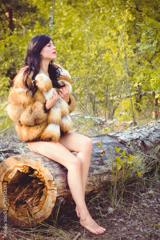 Young woman in luxurious furs with a naked body in the forest against a background of nature ...