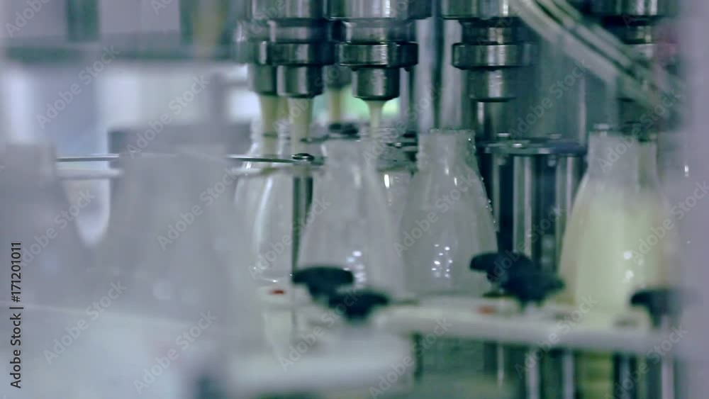 Manufacturing process at milk factory. Milk is pouring into bottle at ...