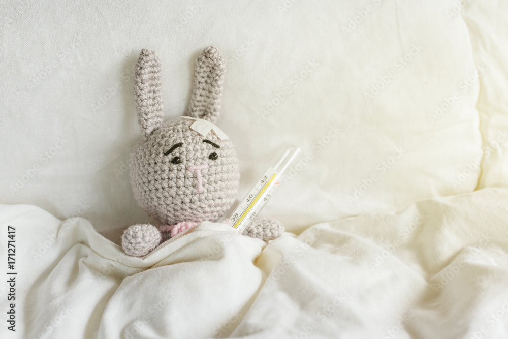 Ill Grey toy rabbit with thermometer and plaster on head in white ...