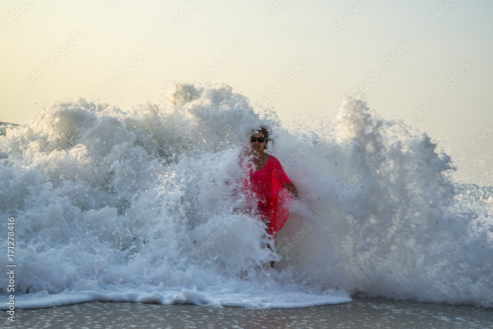A wave of two meters surprises a young woman on the seashore/ A young ...