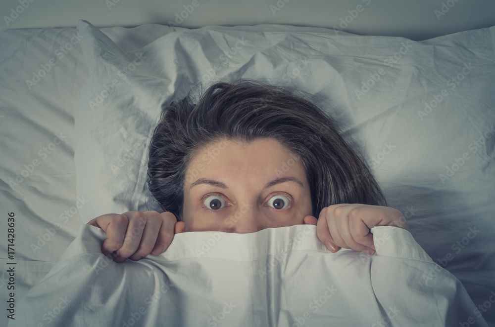 Scared young woman lying in bed and hiding under the sheet Stock Photo ...