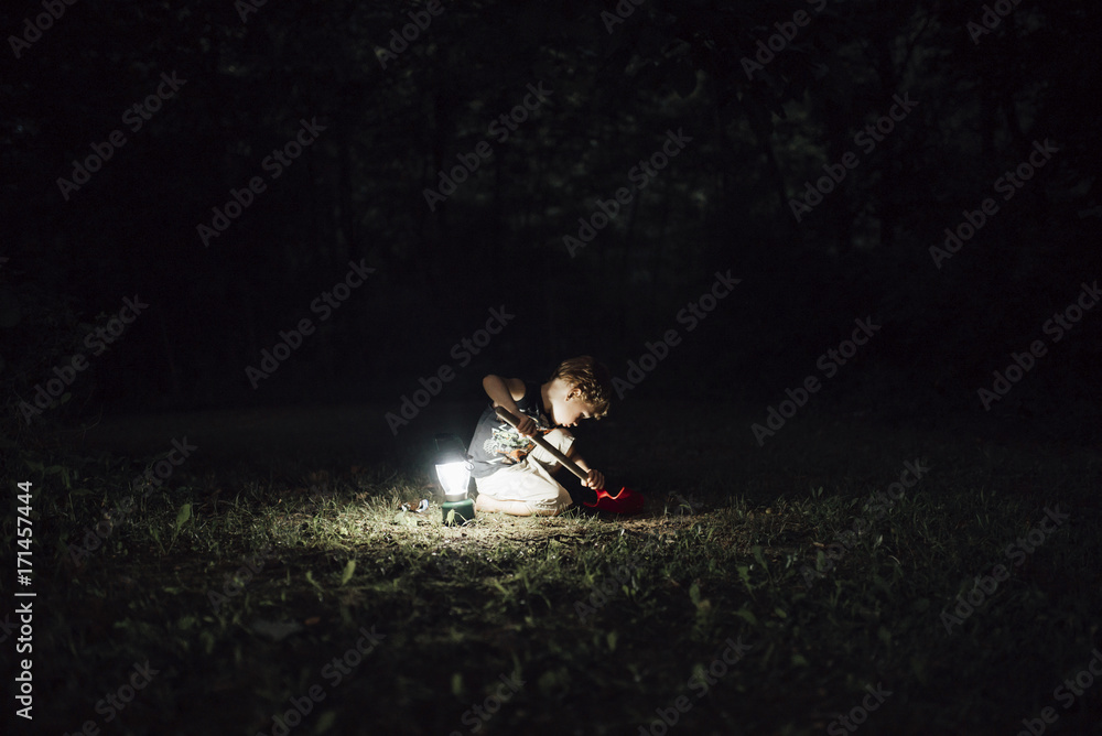 Boy digging soil with shovel at yard by illuminated lantern during ...