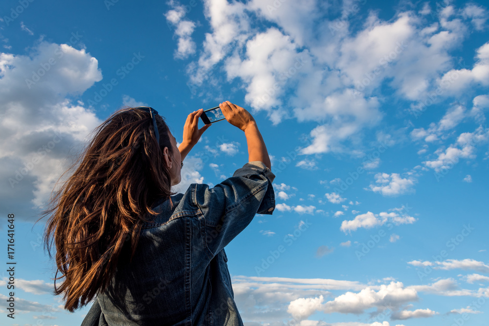 Beauty young woman taking pictures of a cloudy sky with a smartphone ...
