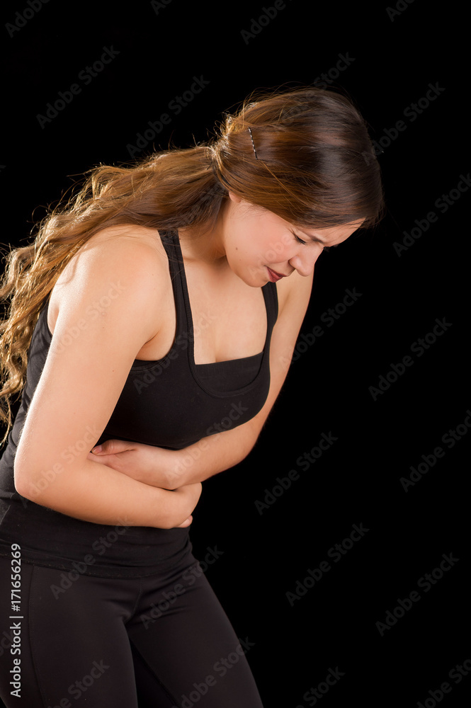 Beautiful young woman with stomach ache or nausea in a black background ...