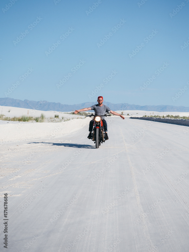 Young man riding classic motorcycle with no hands through White Sands ...