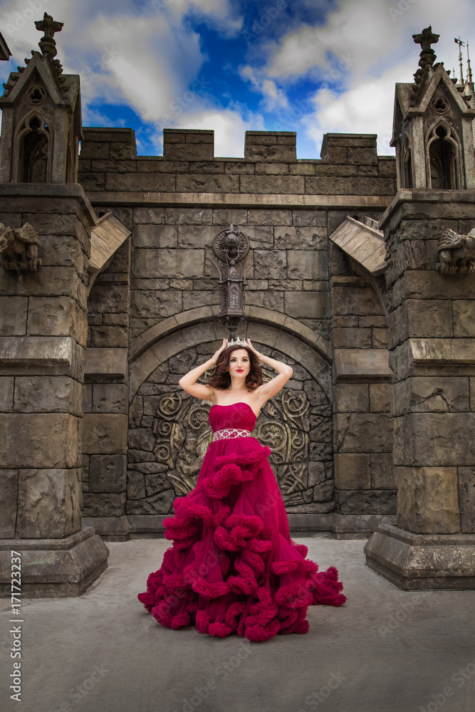 A beautiful woman, a queen in a red luxurious dress, stands on the ...
