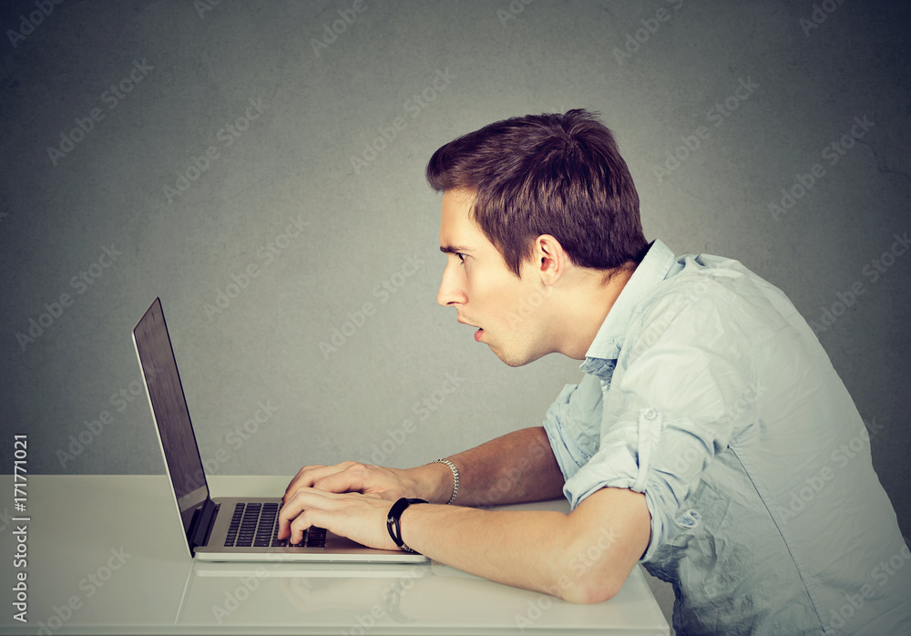 Shocked perplexed man sitting in front of laptop computer looking at ...