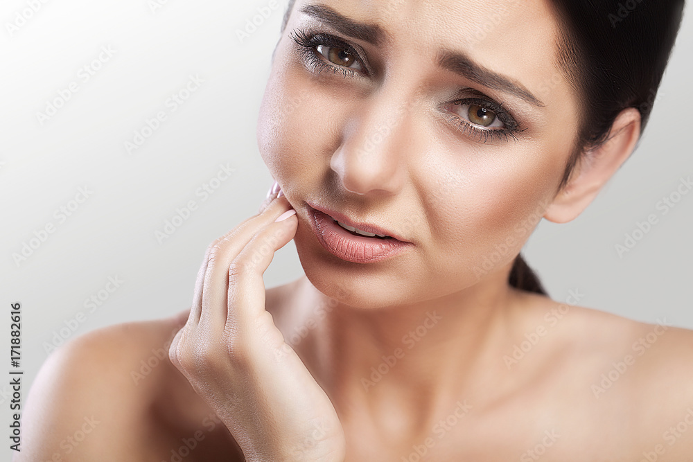 Beautiful young woman suffering from a toothache on a gray background ...