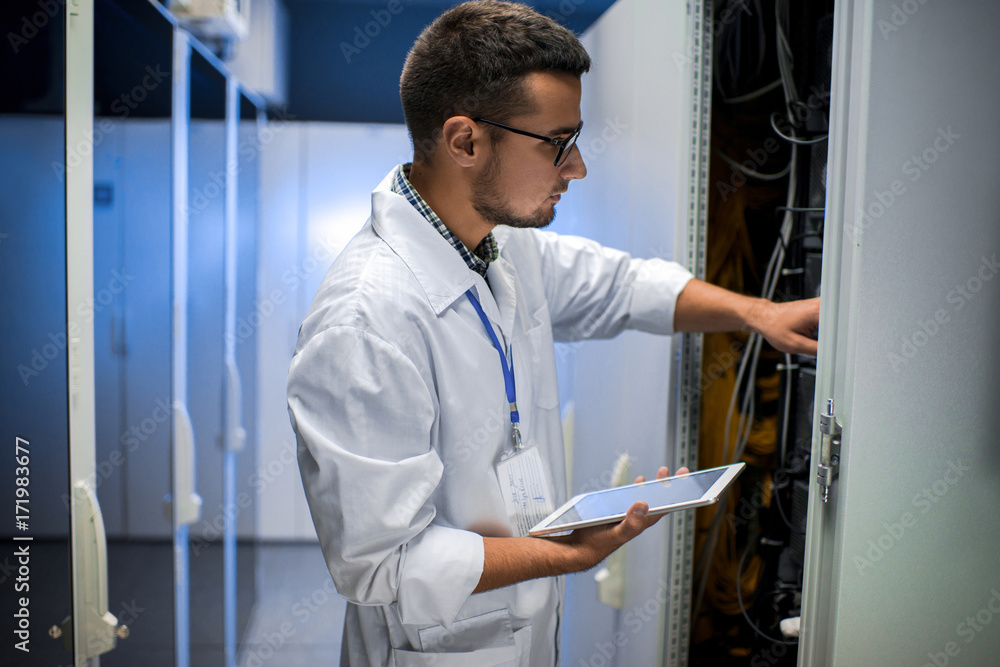Side view portrait of young scientist looking in server cabinet while ...