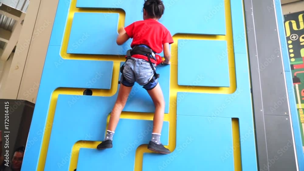 Courage little girl climbing a wall indoor while wearing a safety rope ...