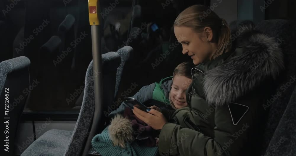 Mom and son having a night bus ride. To pass the time they using mobile ...