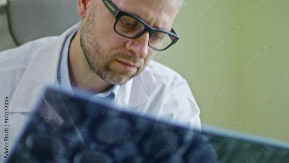 Tilt down of concentrated doctor in glasses looking at MRI scan of ...