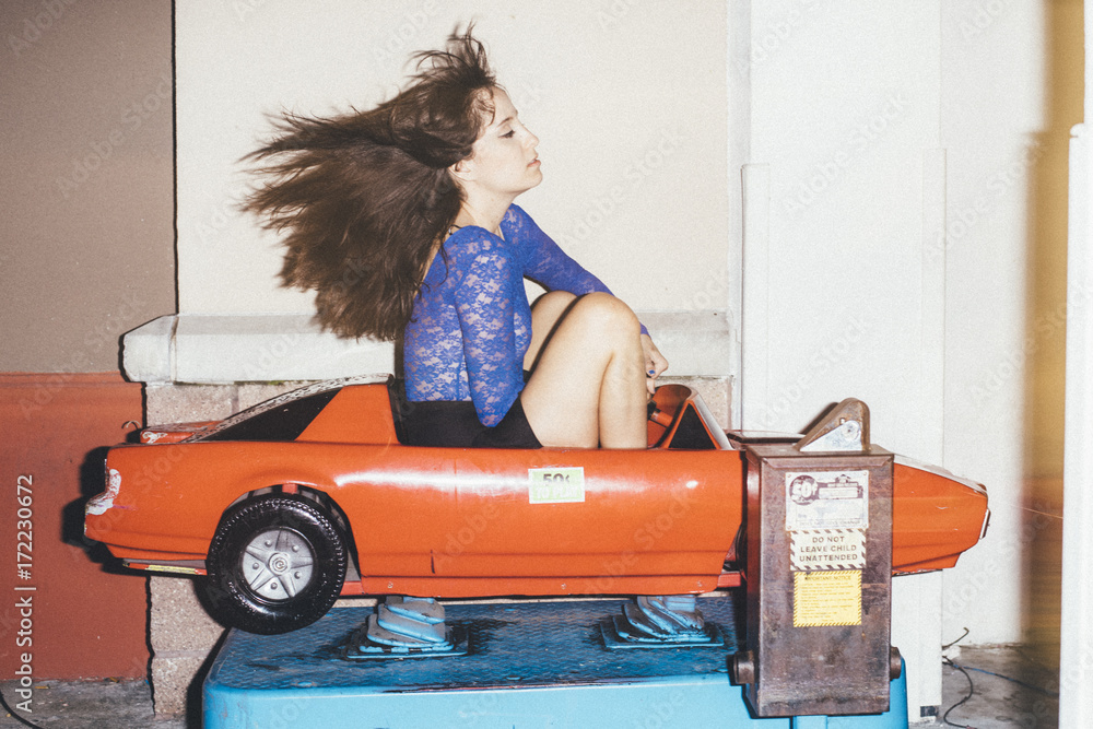 Woman fashion model posing and riding coin operated car ride at night ...