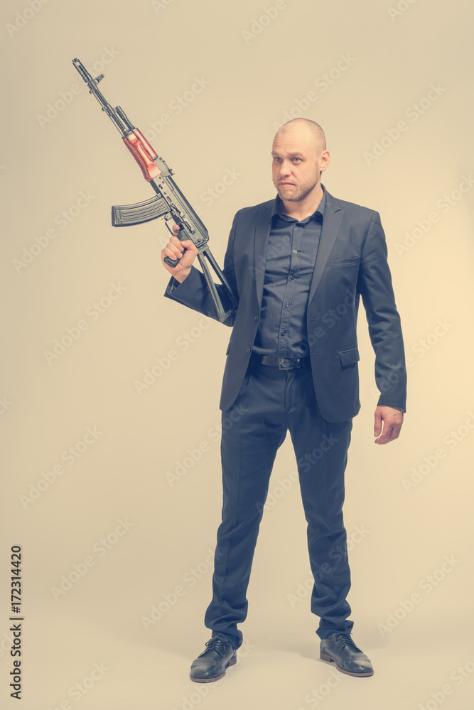 Bald man in a gray suit holding a gun. Toned Stock Photo | Adobe Stock