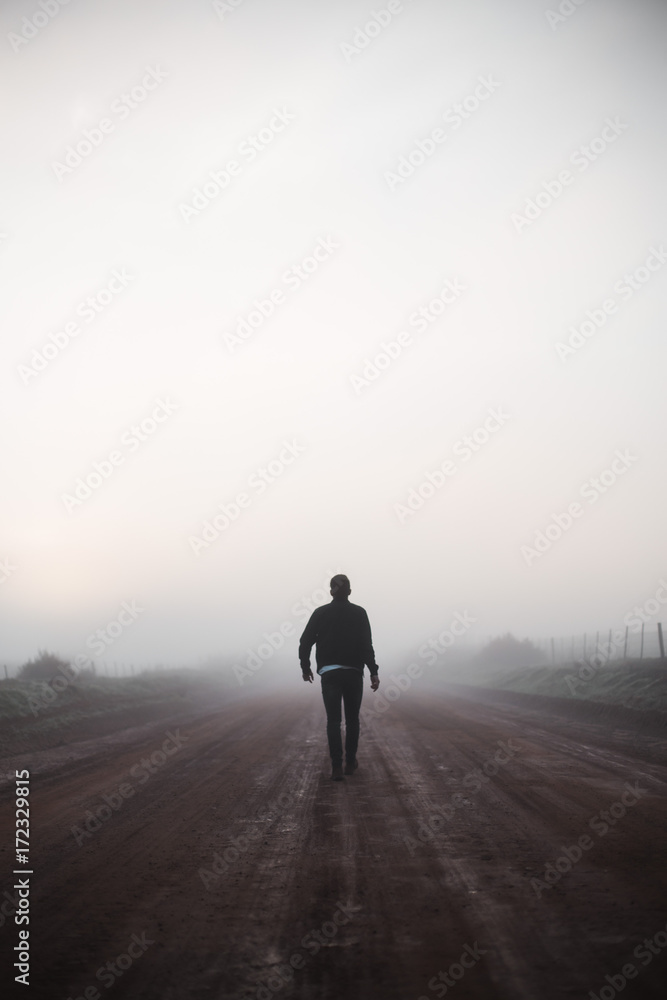 Silhouette man walking into mist on dirt road Stock Photo | Adobe Stock