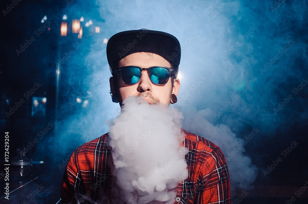 Punk man in the vape shop is sitting at the bar and smoking a ...