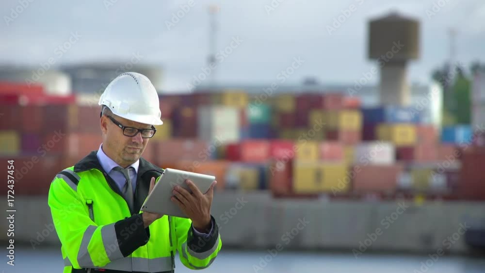 A foreman planning logistics, using a tablet, in front of a container ...