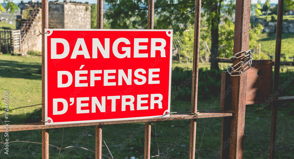 red sign placed on a rusty gate or it is written in French danger ...