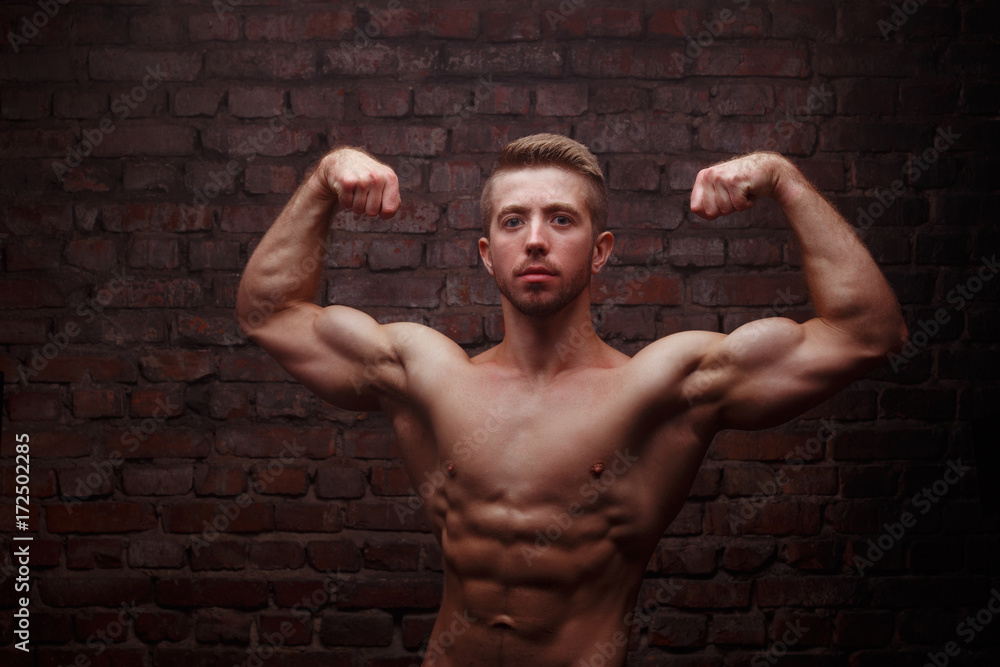 Young fit man bodybuilder with perfect big muscles posing over brick ...