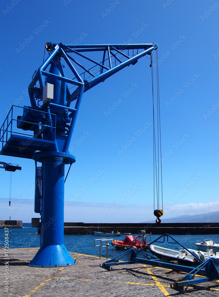 blue tower crane in a harbor dockyard with sea and boat dockside wall ...