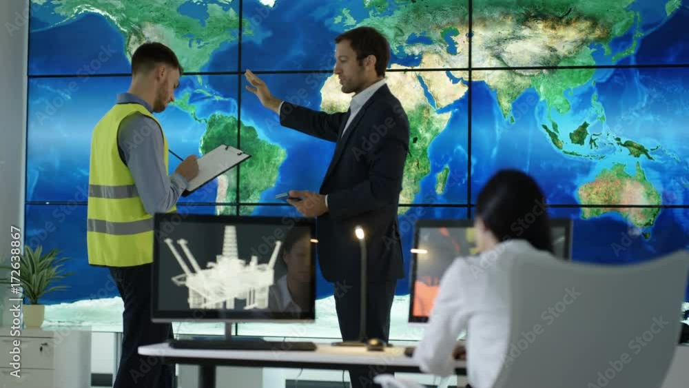 Engineering team in discussion looking at large world map graphic on ...