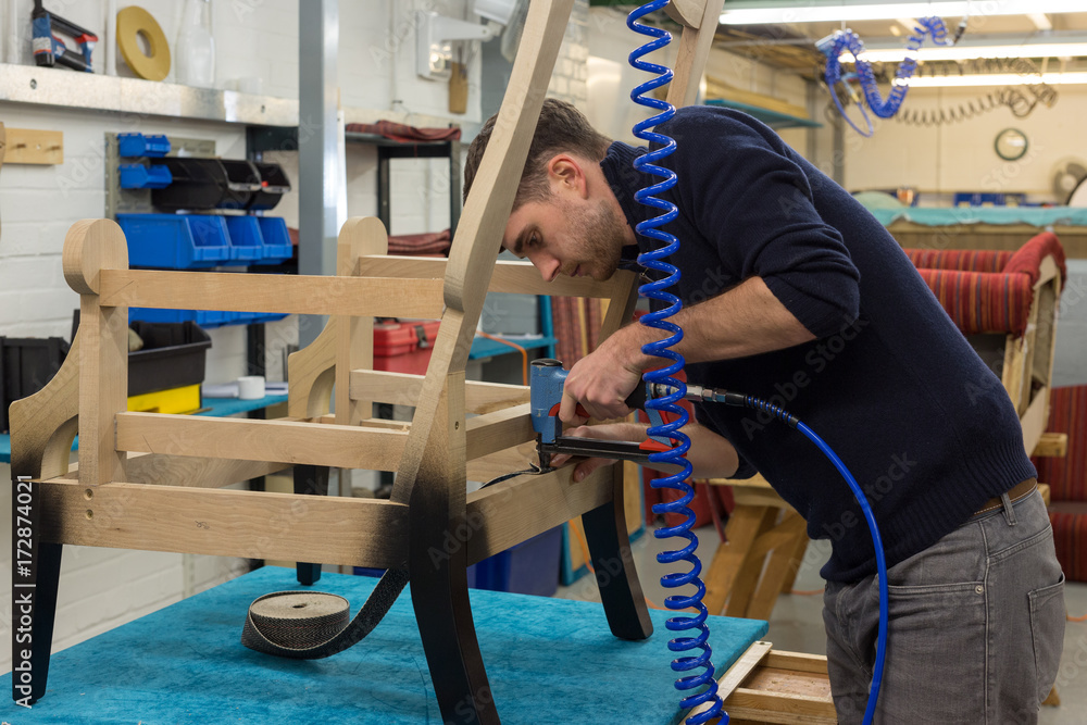 Craftsman renovating an armchair using webbing and a pneumatic stapler ...
