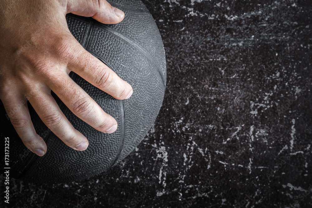 Man's hand dribbling an old, black basketball ball on the dark floor ...