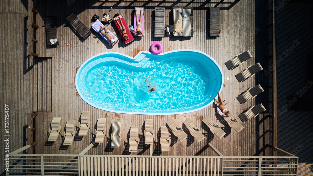 top view of few female tanning near blue pool with pink inflatable ring ...