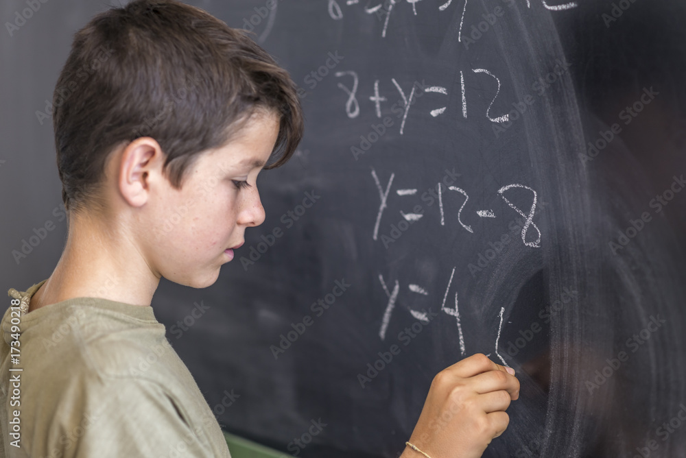 Schoolboy solving a problem on a blackboard. Stock Photo | Adobe Stock
