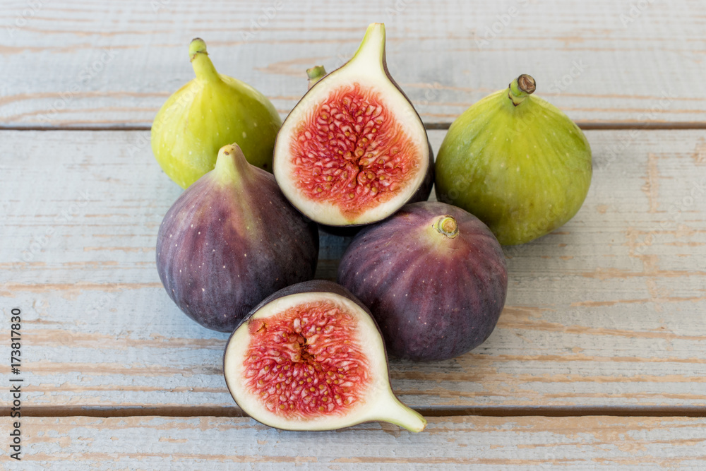 Whole figs and one fig sliced in half on top of a garden table. Focus ...