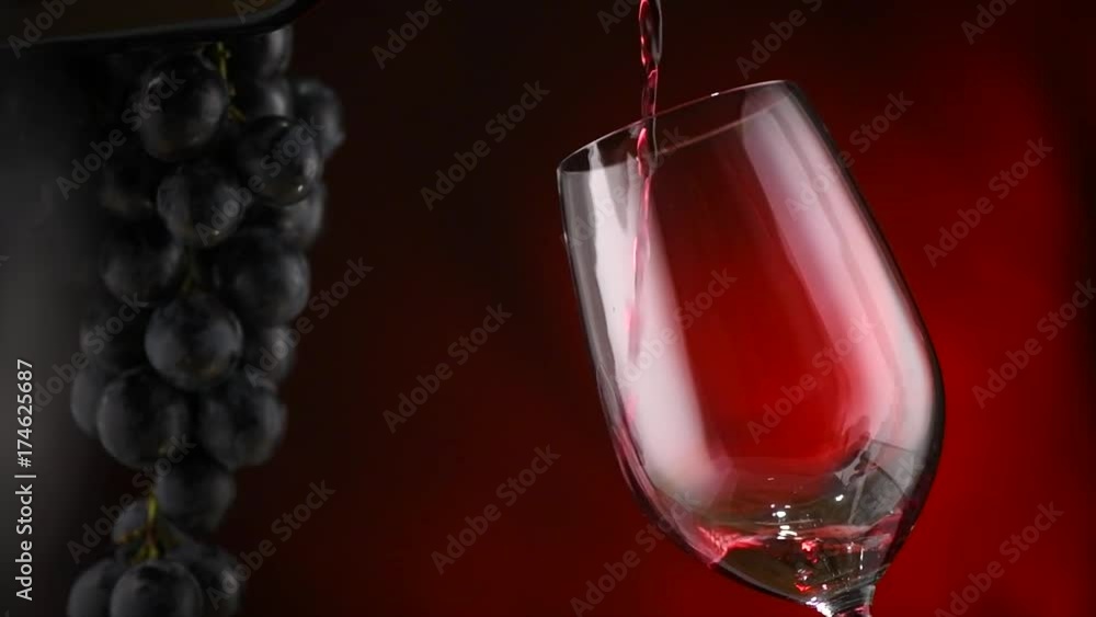 Wine. Red wine pouring in wine glass over dark background. Slow motion ...