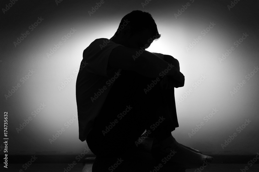 sad silhouette of a man in depression sitting on a chair with his head ...