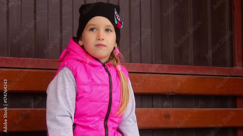 Little girl sitting on a bench waiting for transport at the bus stop ...