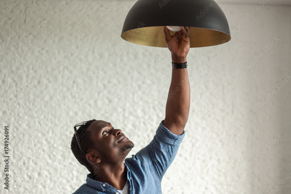 African man changing light bulb , installing a fluorescent light bulb ...