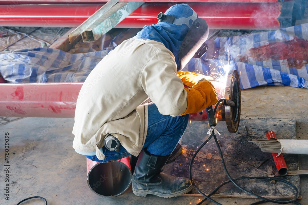Construction worker welding red steel pipe for fire alarm system in new ...