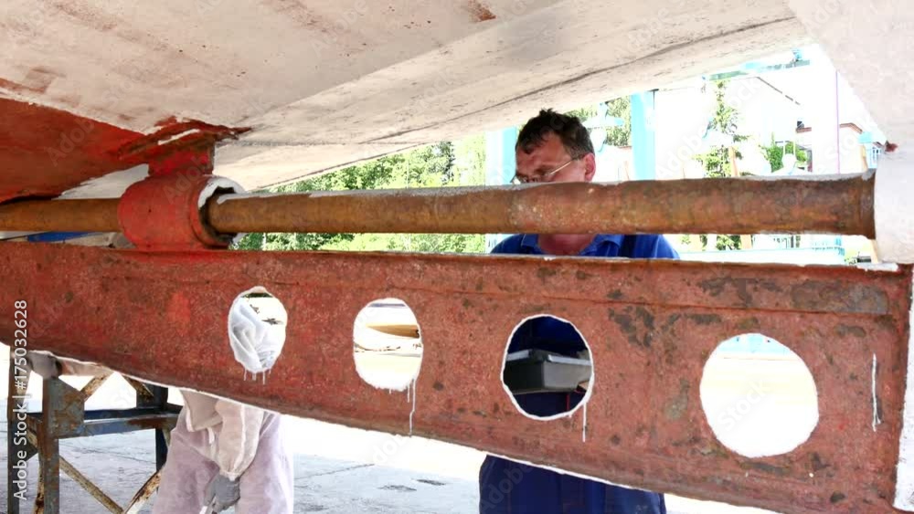 Worker paints with brush metal of rusty ship at shipyard in port of ...