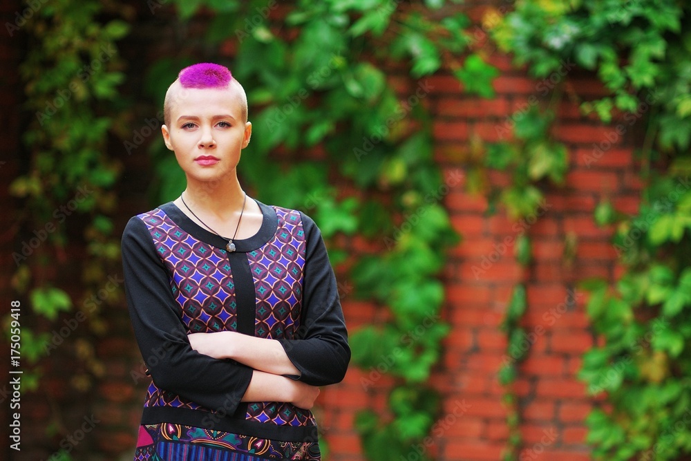 Beautiful punk girl with a purple mohawk standing against a background ...