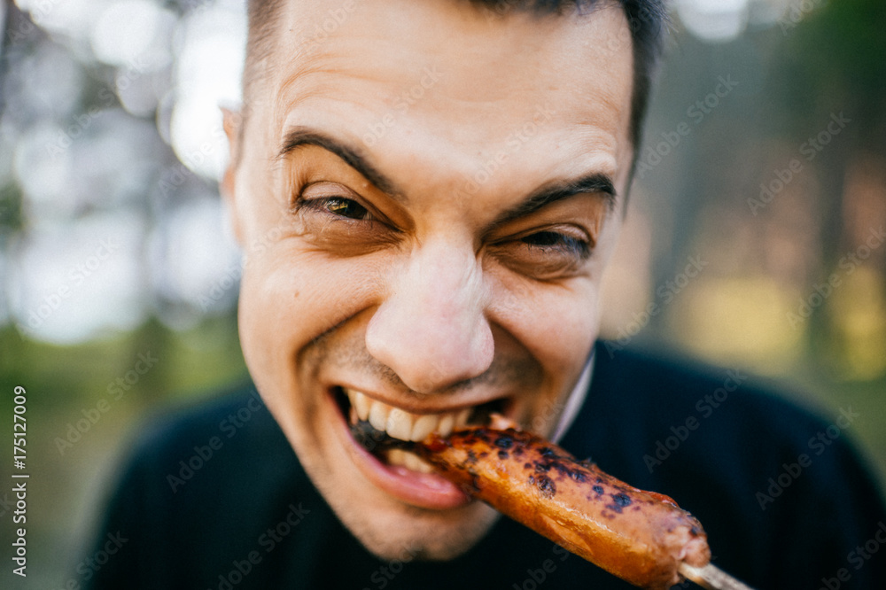 Closeup portrait of male licking and biting roasted sausage with ...
