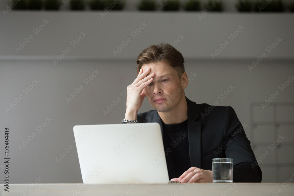 Exhausted businessman looking at laptop with hand on his forehead ...