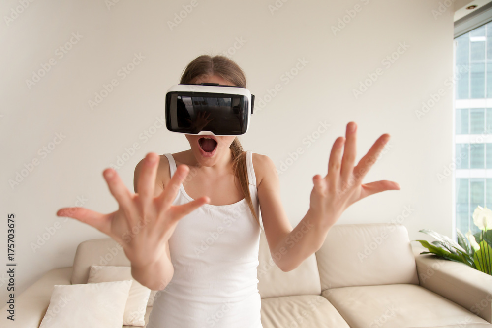 Surprised amazed young woman wearing VR glasses looking at her own ...