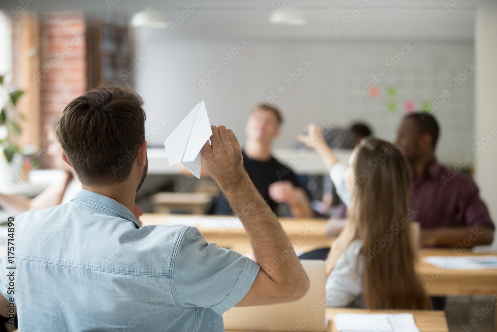 Rear view of company employee launching paper plane towards coworker ...
