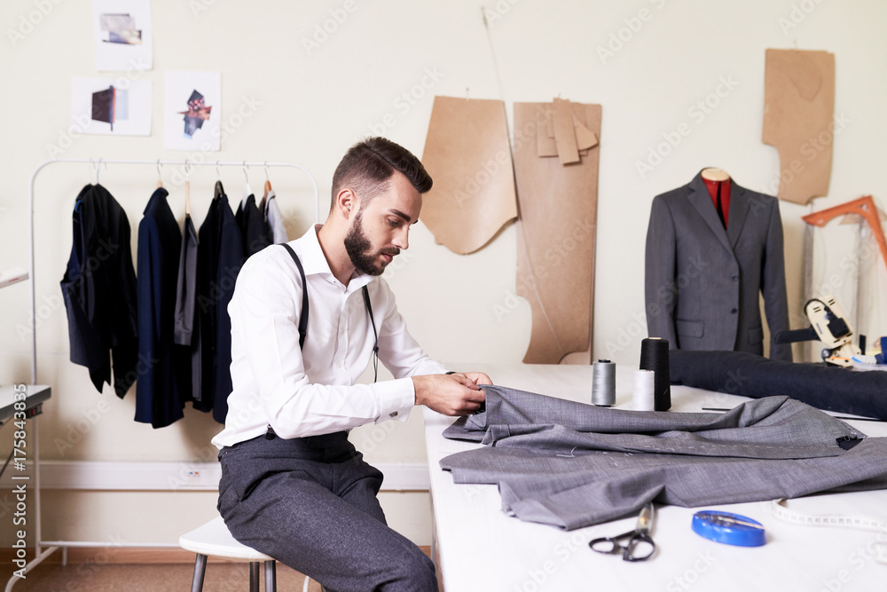 Side view portrait of handsome young man sewing bespoke suit at table ...