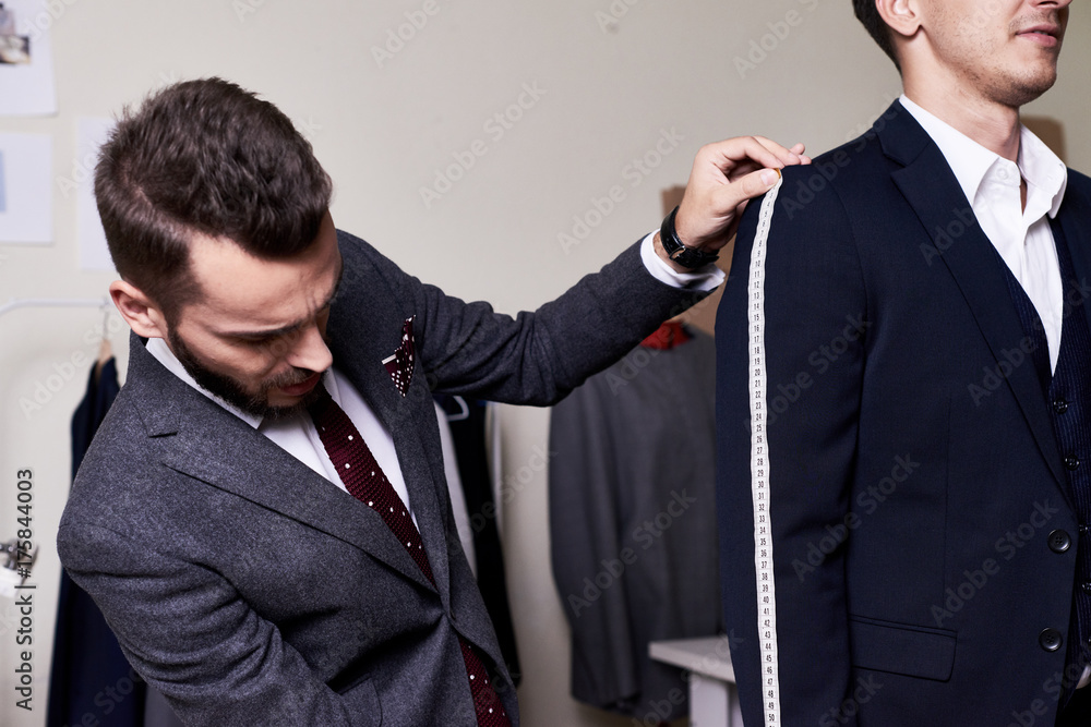 Portrait of modern tailor measuring arm length of bespoke suit during ...