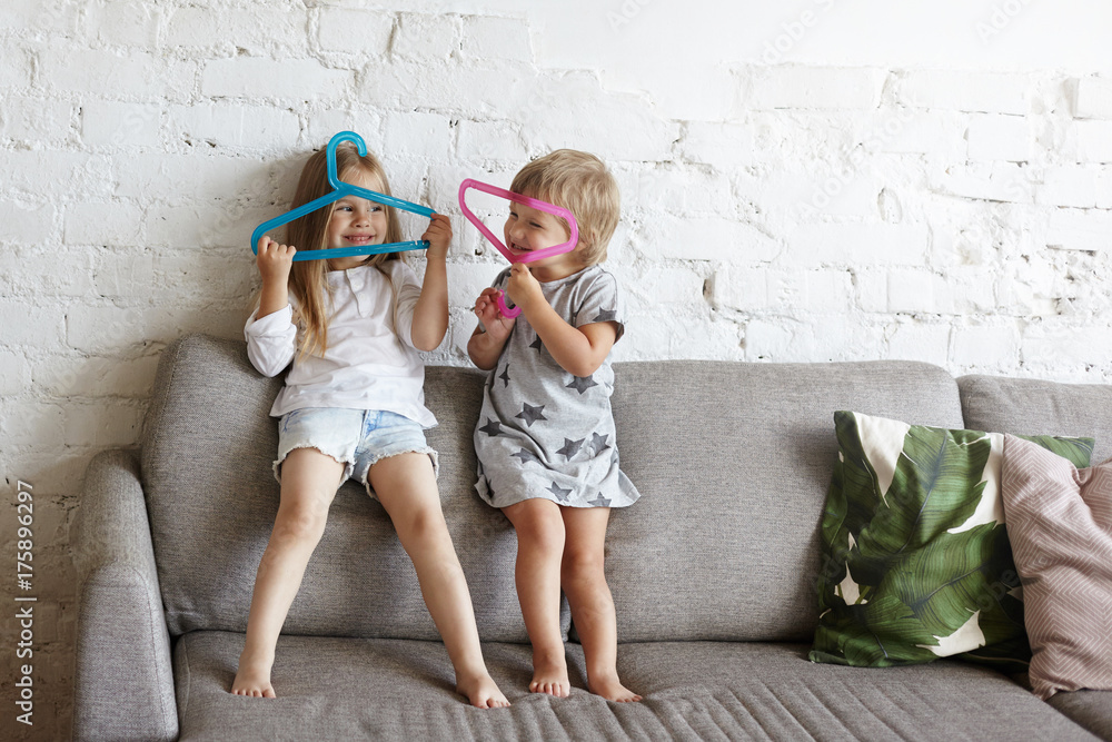 Candid shot of two mischievous little girls standing barefooted on grey ...