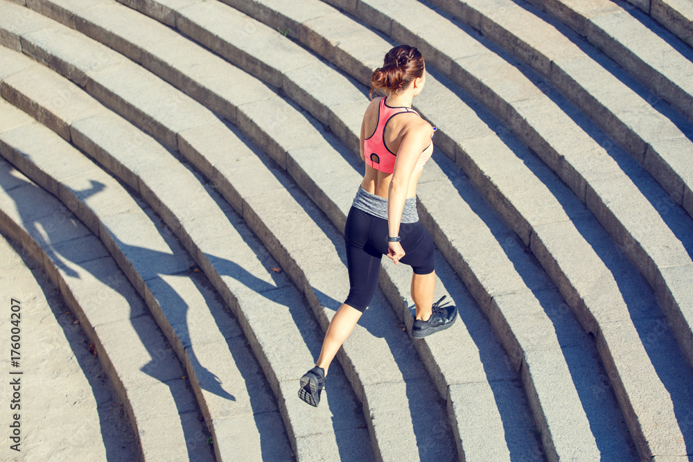 Young slim woman in pink top running up on stairs in the morning city ...