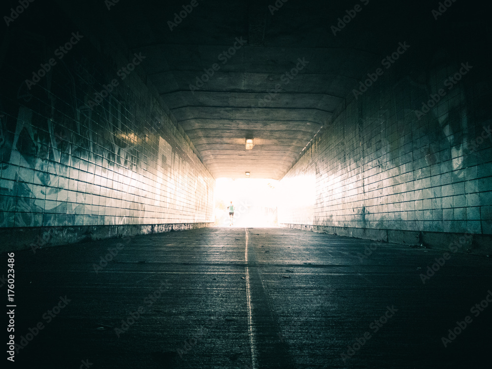 Woman running through tunnel towards bright light Stock Photo | Adobe Stock