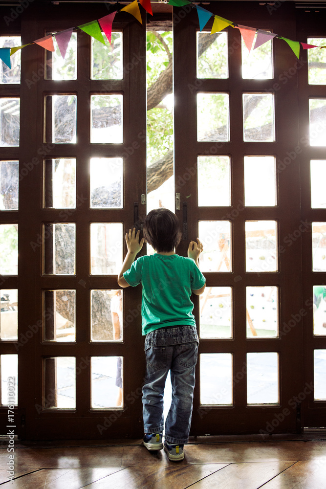 Young child peering through sliding glass door with wooden frames ...