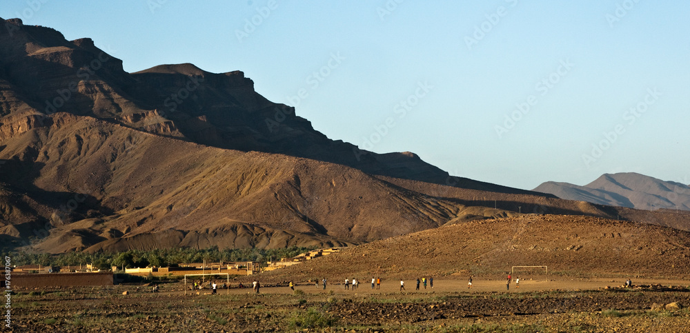 people playing football in a dirt football field in the Moroccan desert ...