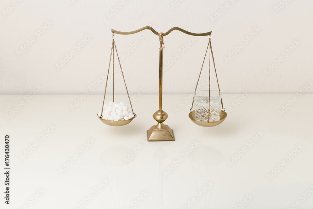 Gold brass balance scale with sugar and glass of water on white glass ...